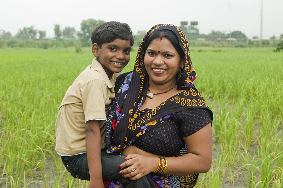 Smiling Rural Villager Mother holding his-Son in his-arms Standing In-farm